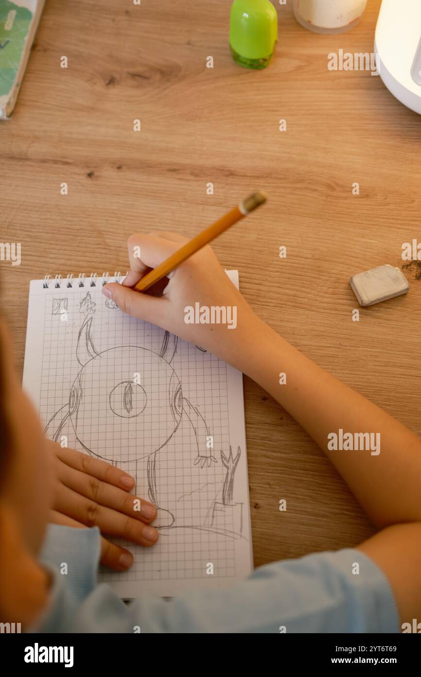 Child sketching a creative monster design on graph paper at their desk ...