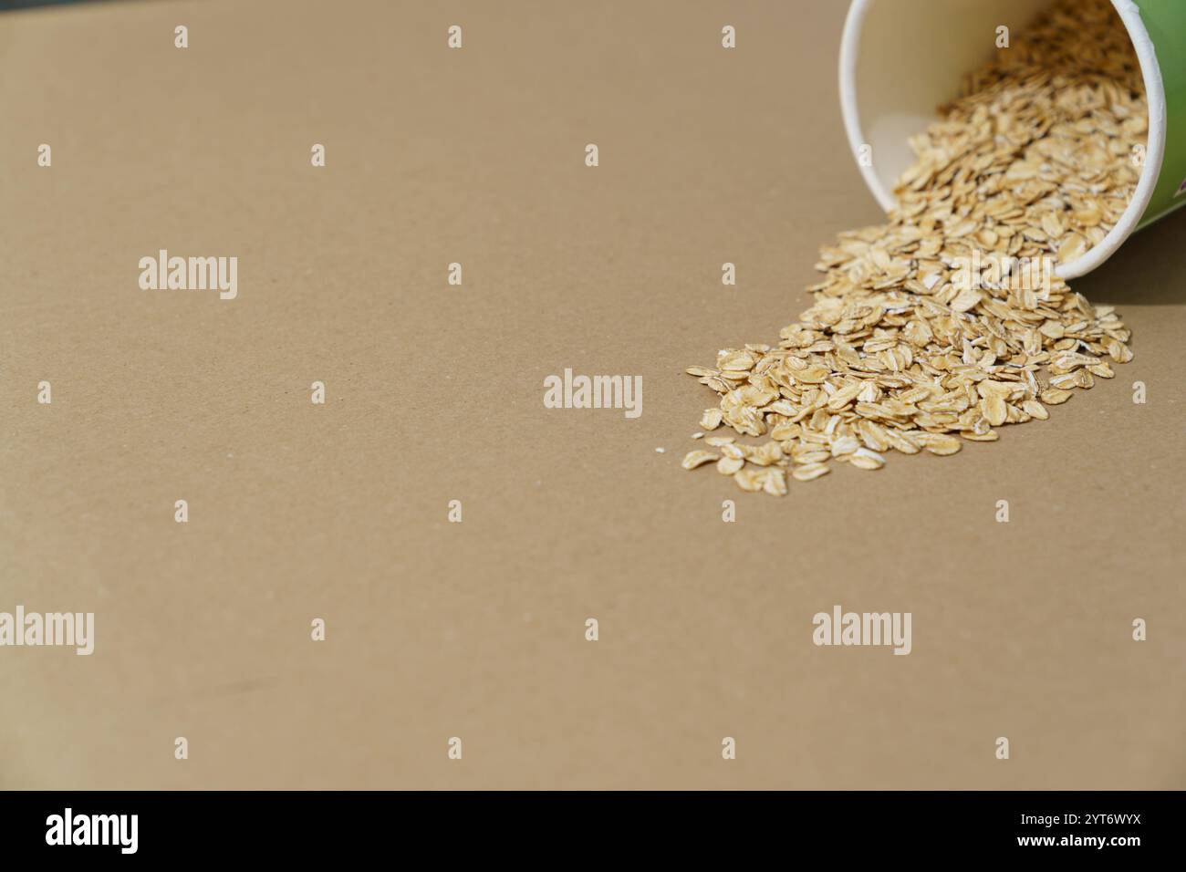 A container with spilled dry oatmeal onto a brown paper background with ...
