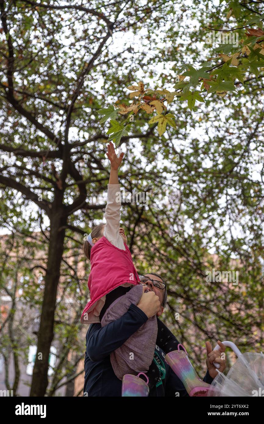 A father lifts his daughter high in an autumn park as she reaches for ...