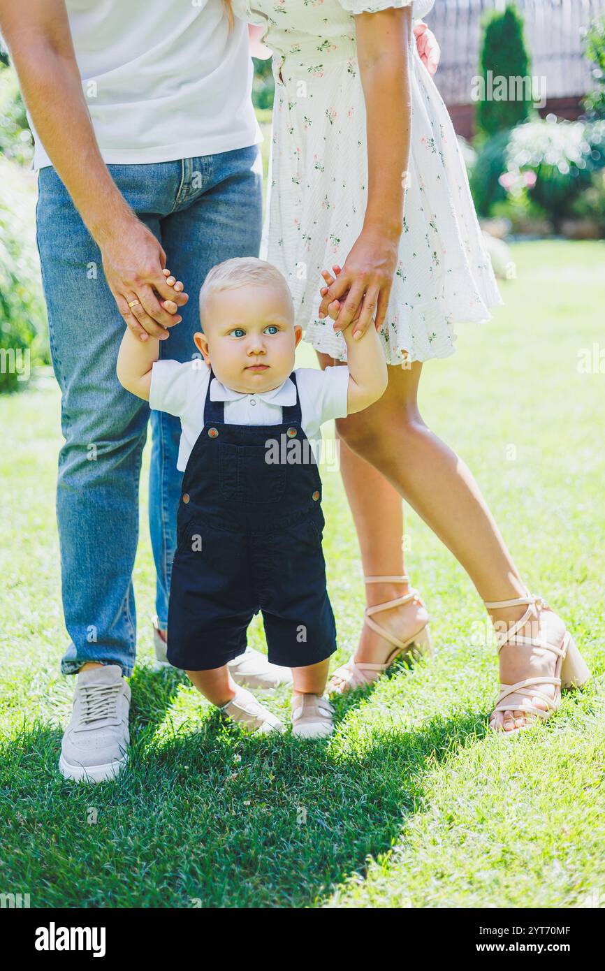 Little boy learning to walk holding hands with mom and dad. Child ...