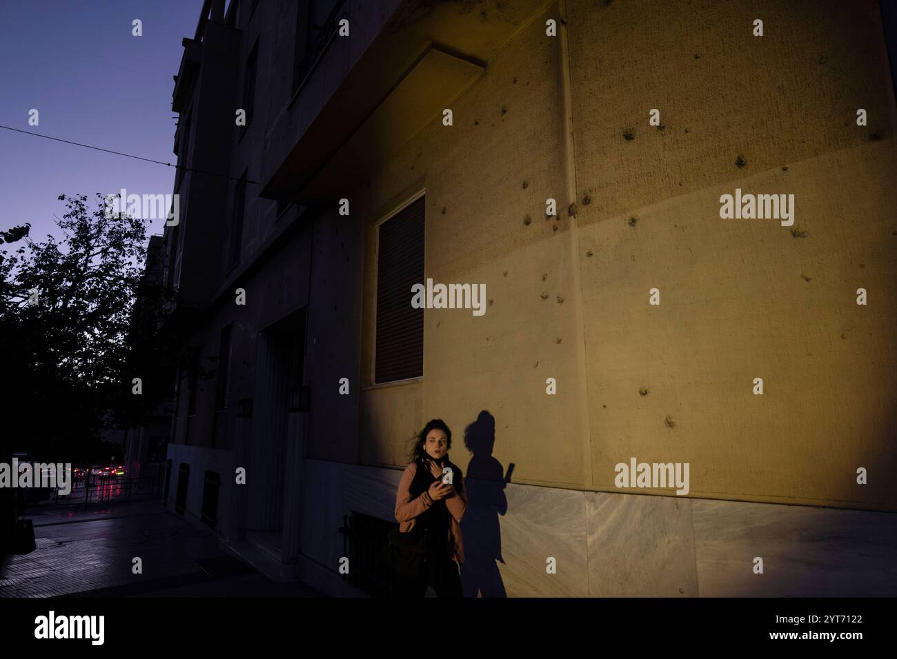 A woman walks next a Bullet-riddled wall of a building in the Greek ...
