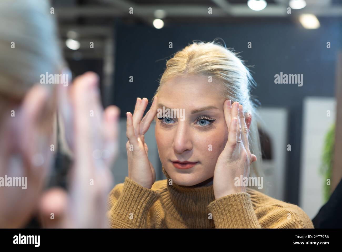 Blonde woman checking her skin in the mirror, touching her forehead ...