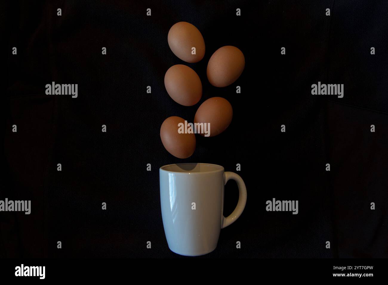 Eggs falling into a white cup on a black background easter Stock Photo ...