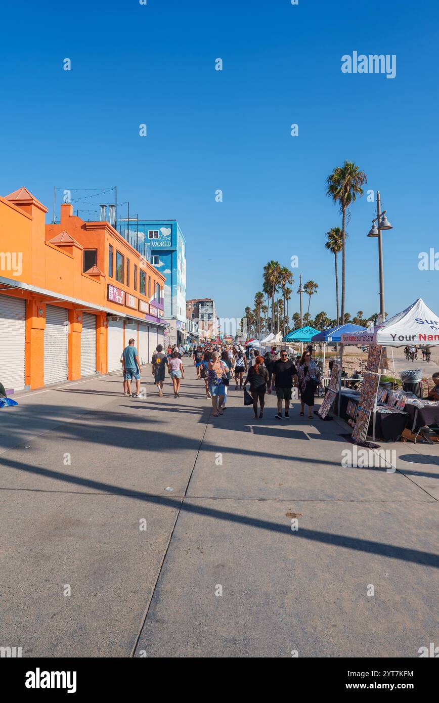 People walk past colorful storefronts and vendor stalls on Venice Beach ...