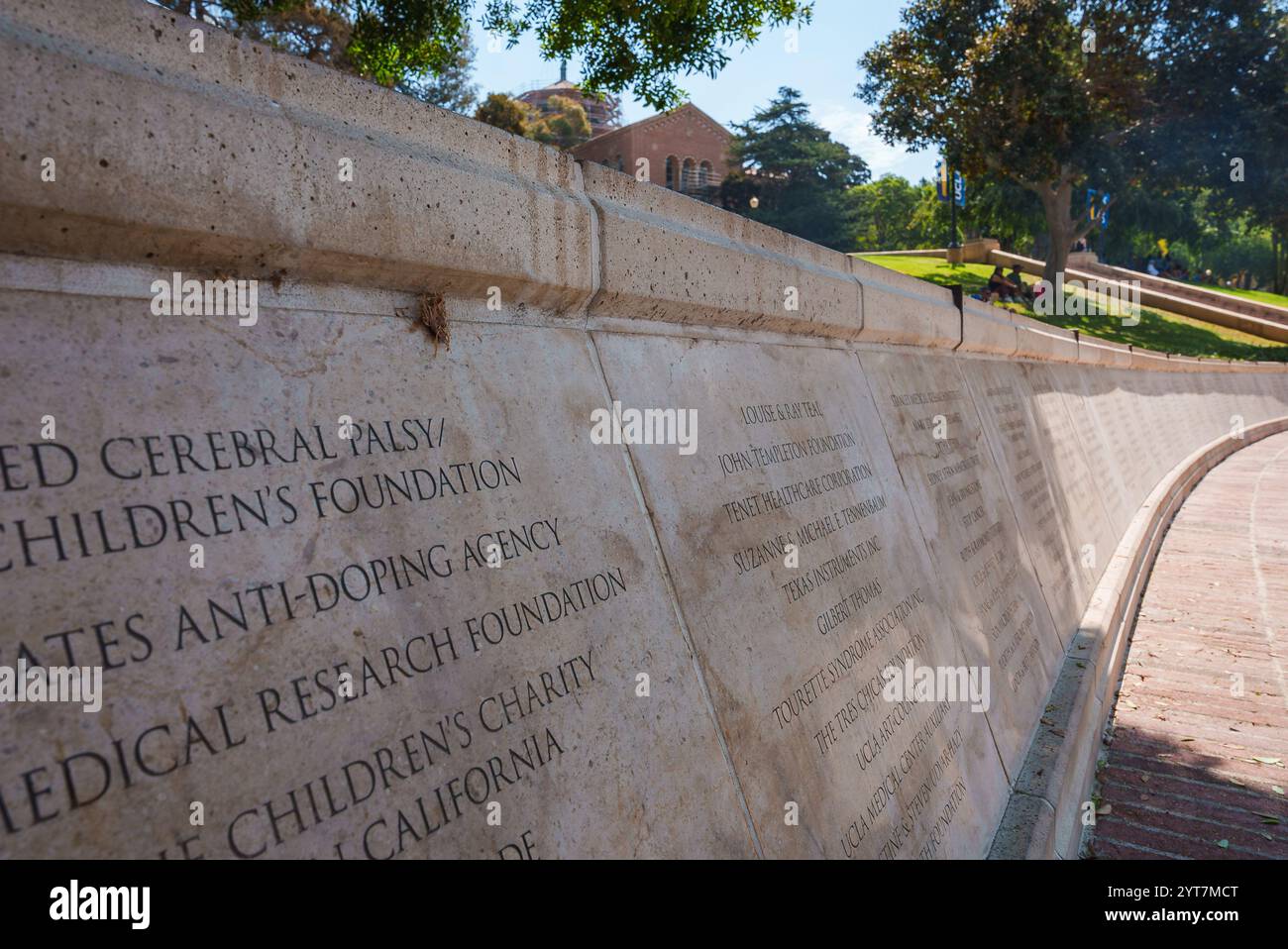 A stone wall with engraved names stands before lush greenery and a ...