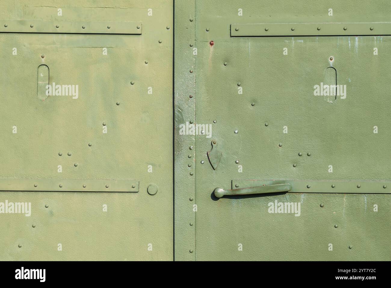 Close-up of a green metal gate with rivets and handle, reflecting ...
