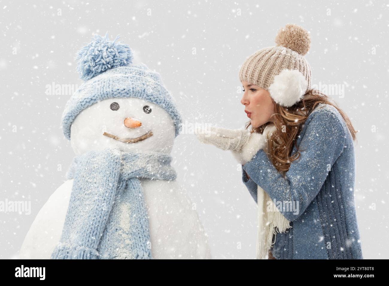 Happy young woman blowing snow from her hands onto snowman in a ...