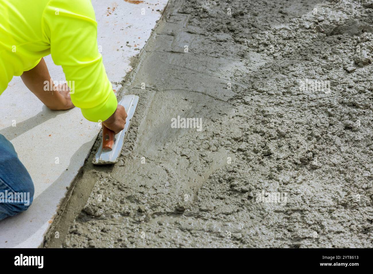 Worker wearing is using trowel to smooth freshly poured concrete ...