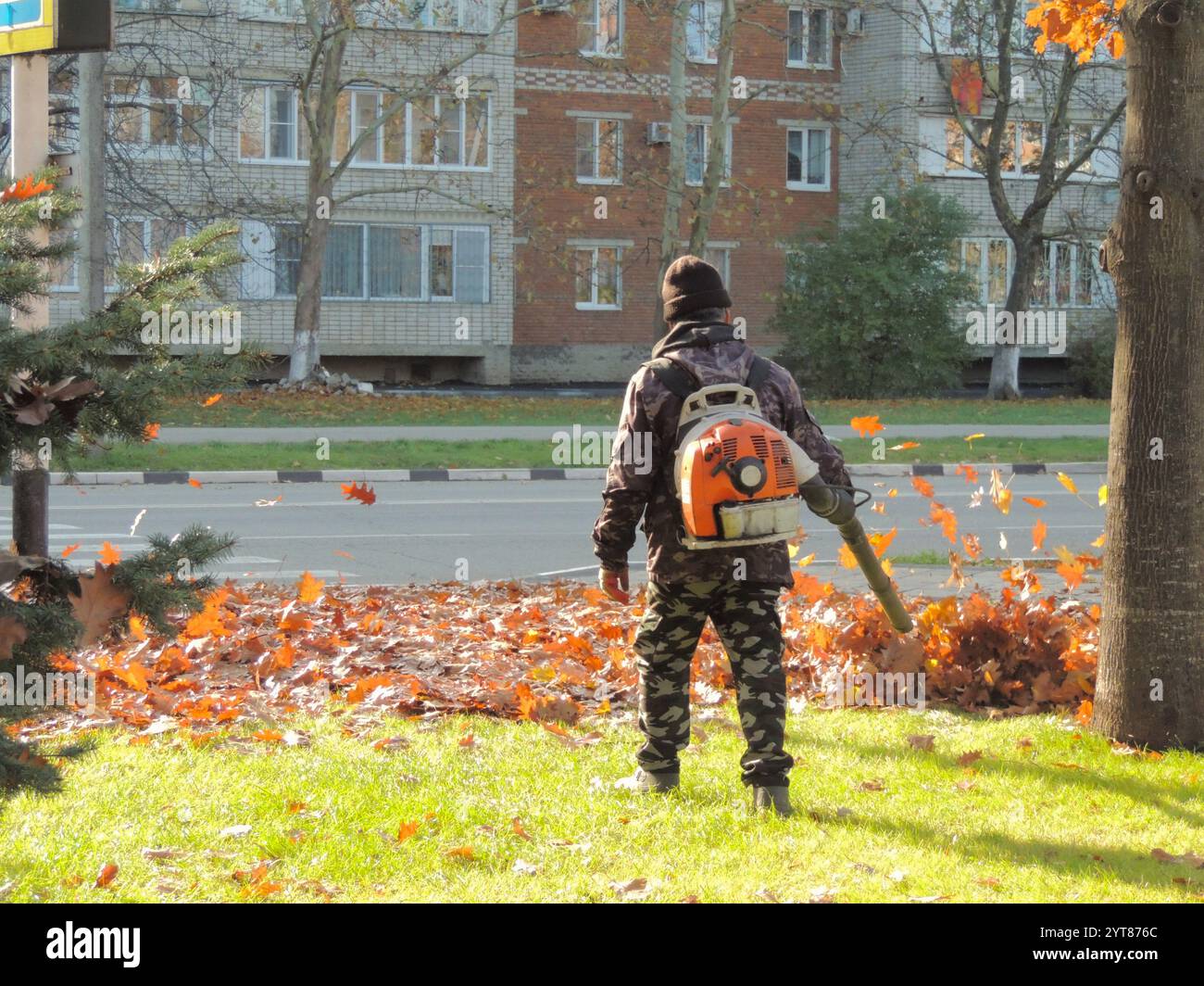 a utility worker from behind in an orange uniform with a vacuum device ...