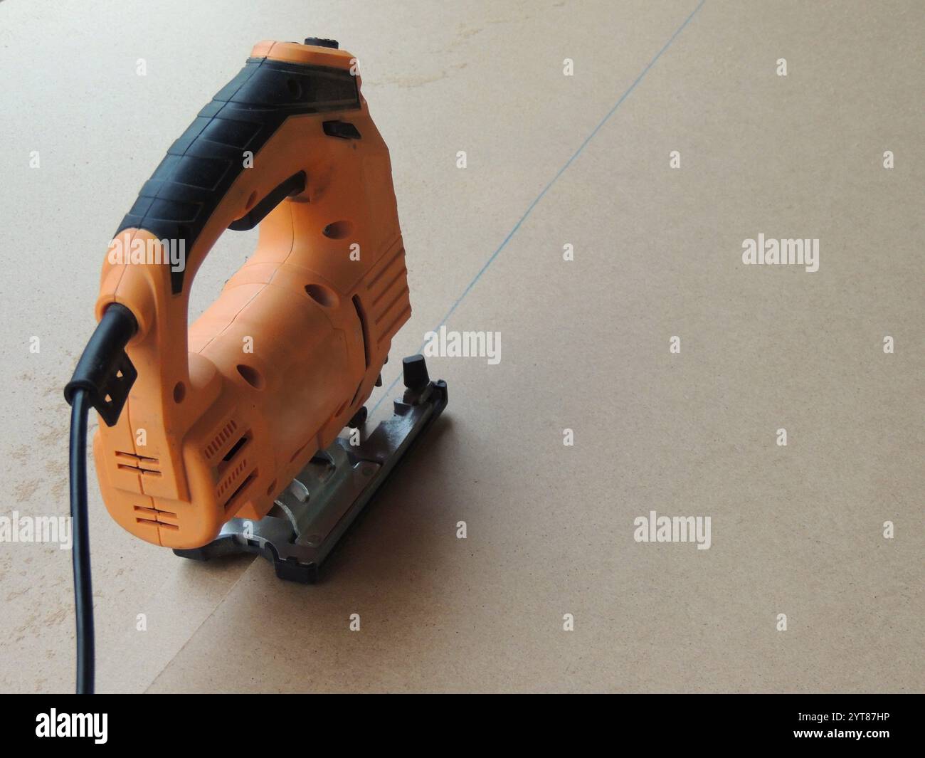 electric orange jigsaw standing on a sheet of plywood or compressed ...