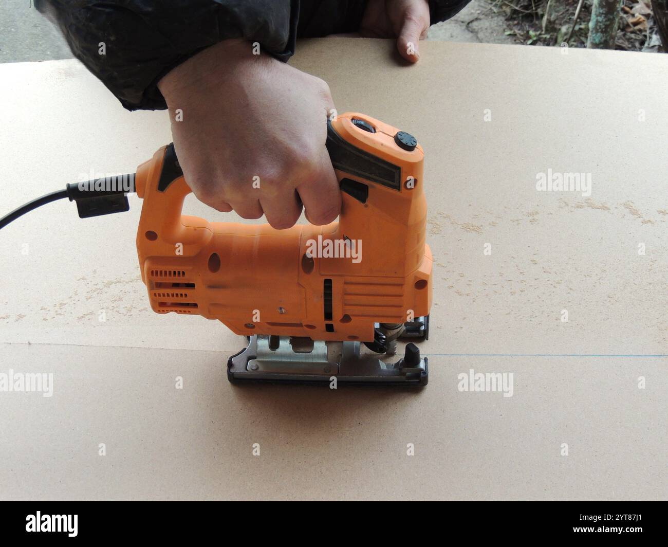 hand holding orange electric jigsaw over large sheet of plywood cutting ...