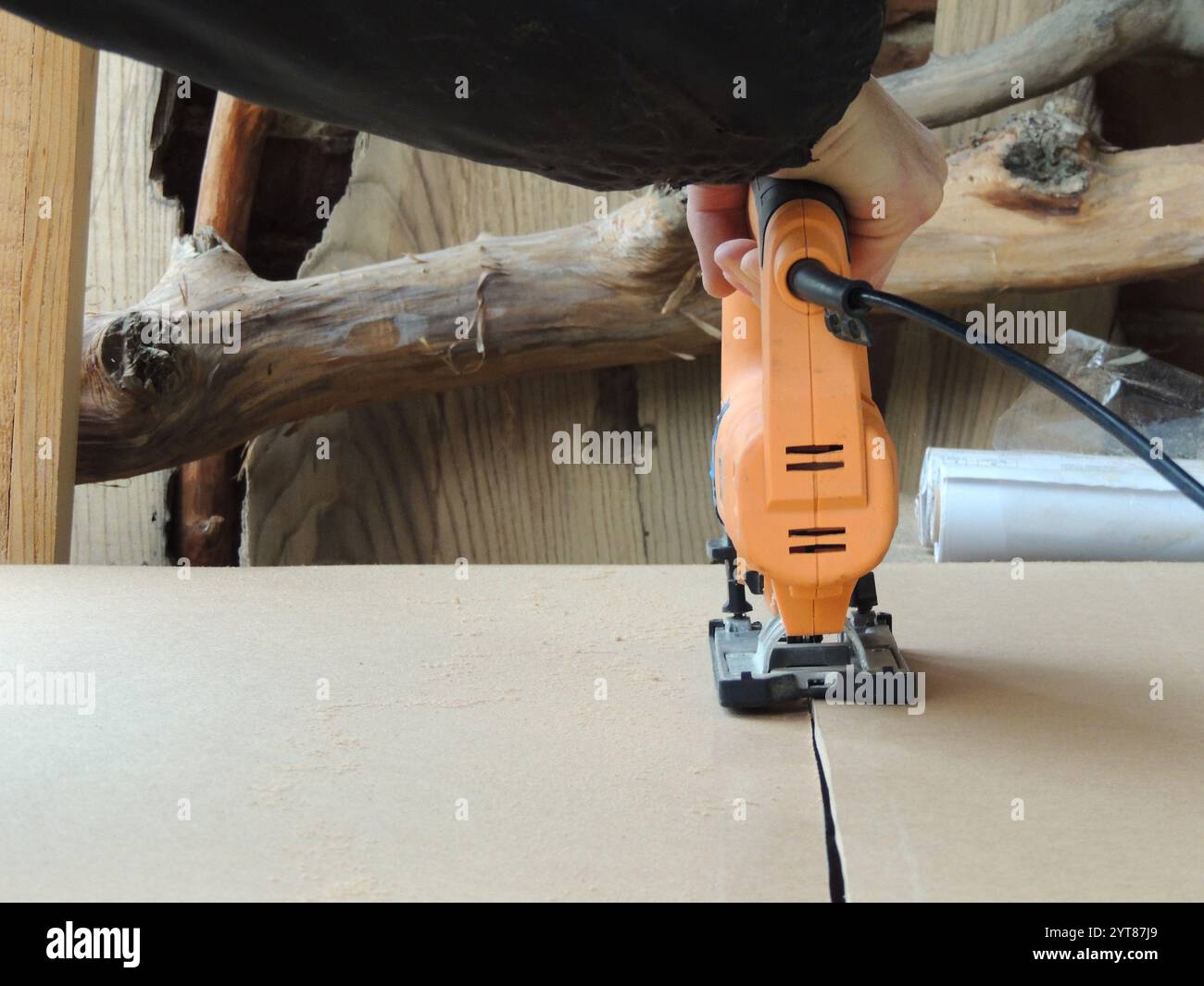 view of orange electric jigsaw cutting large piece of thick cardboard ...