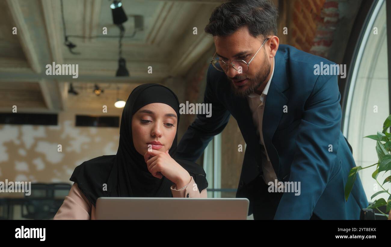 Male businessman teach female muslim worker hijab in office mentor leader help laptop work ...