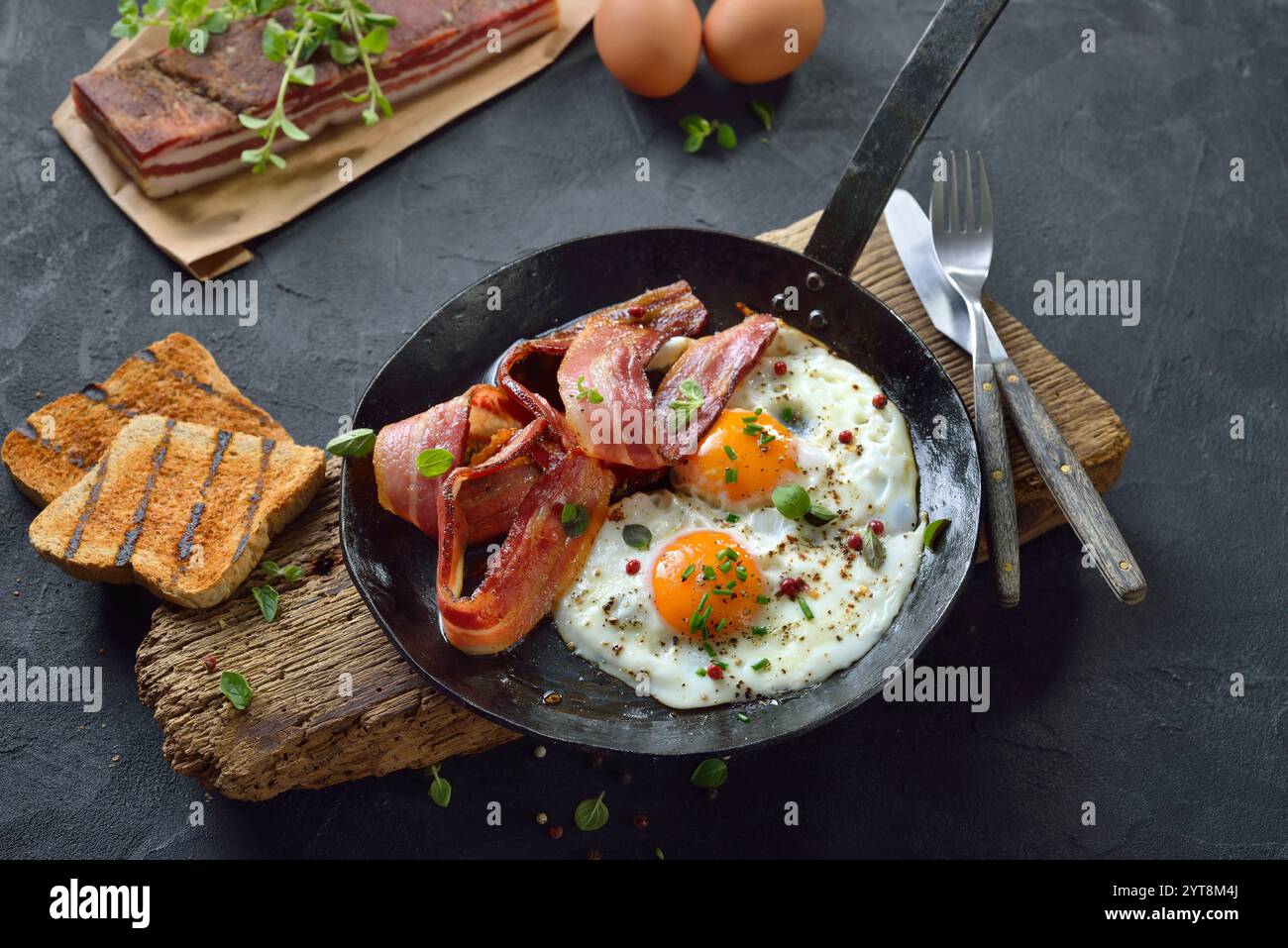 Crispy fried eggs with fried pancetta strips served rustic in an iron ...
