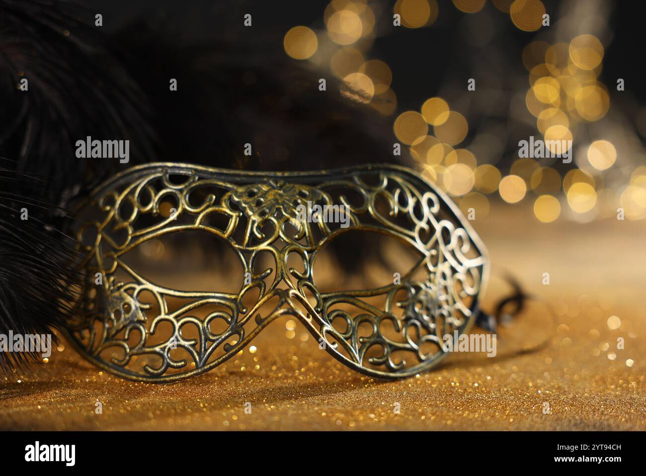 Beautiful carnival mask and black feathers on golden background against blurred lights, closeup ...