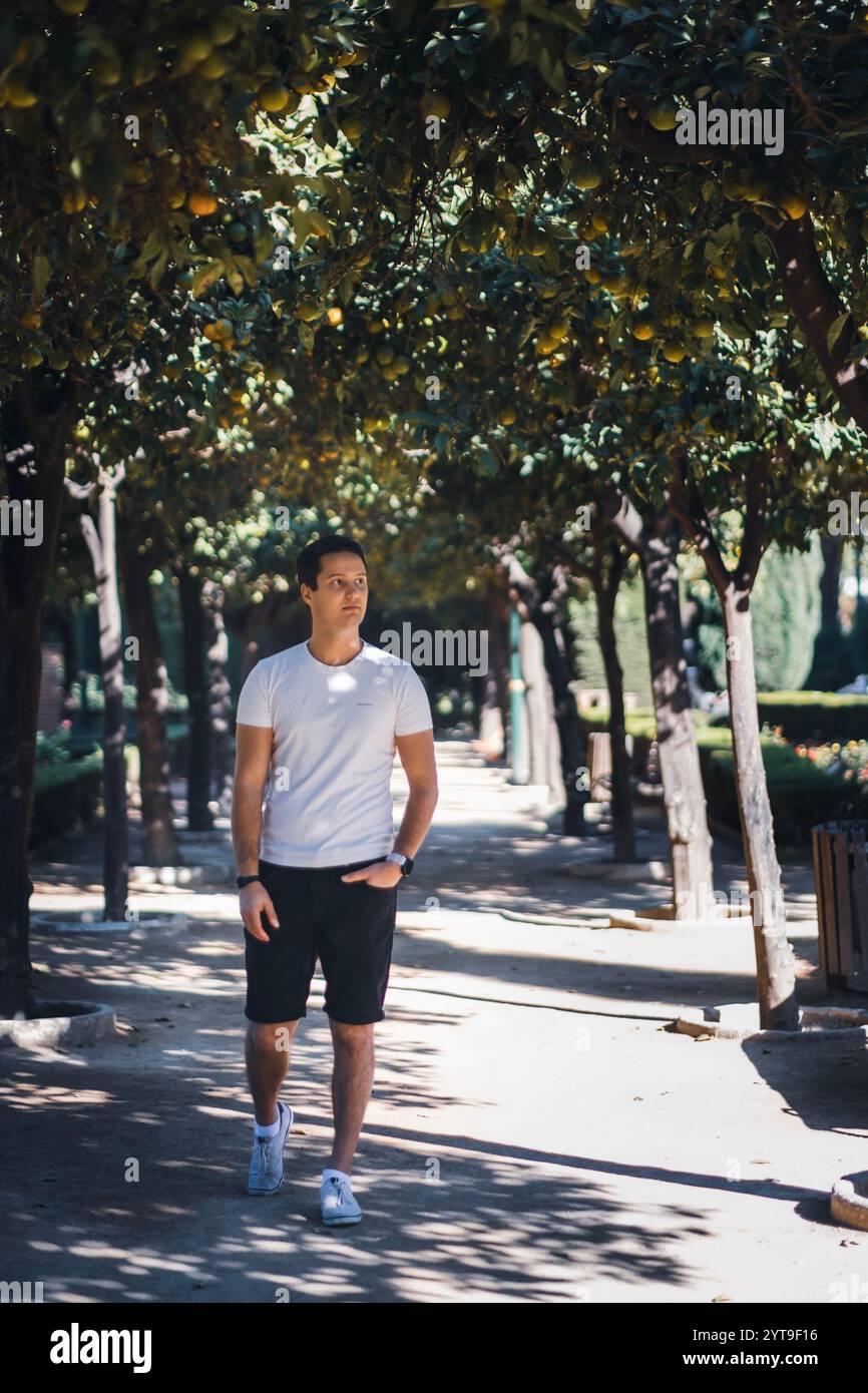 Young man in casual summer attire walking along a tree-lined path in ...