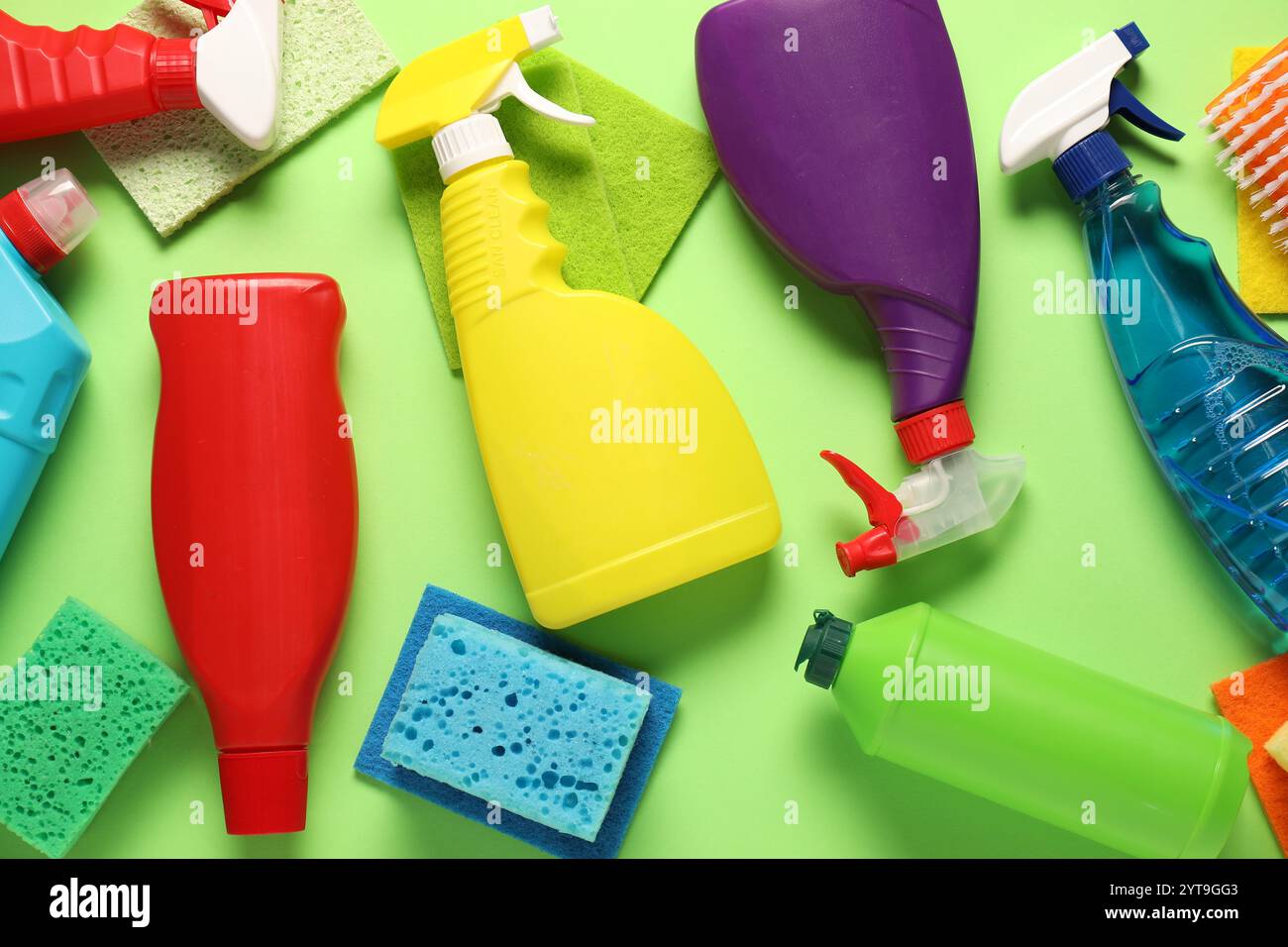 Different cleaning products in bottles and tools on green background ...
