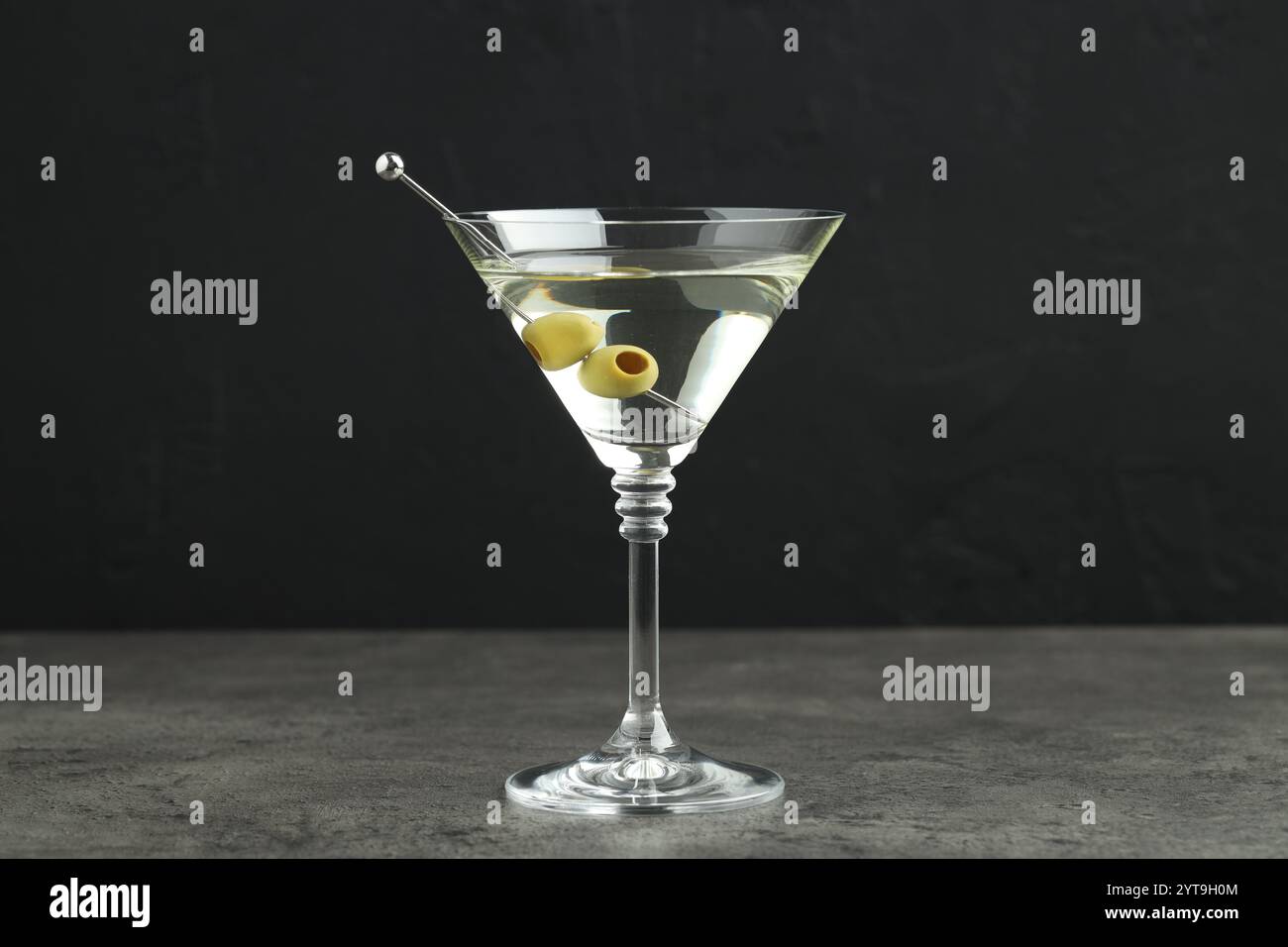 Martini cocktail with olives in glass on grey table against black ...