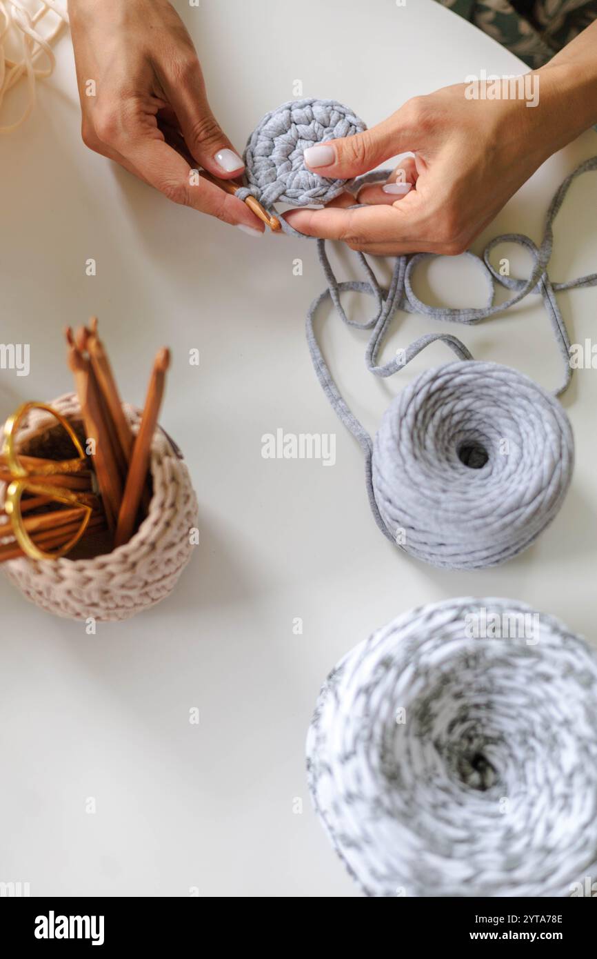 Women's hands crochet with gray yarn on a white background. Skeins of ...