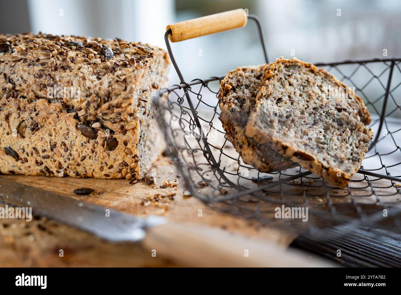 Freshly sliced multigrain bread in basket on wooden cutting board with ...