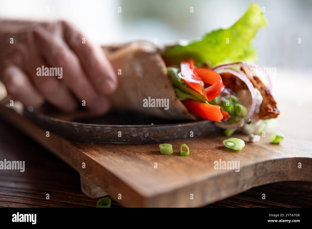 Hand reaches for tortilla wrap with fresh vegatables and fried chicken ...
