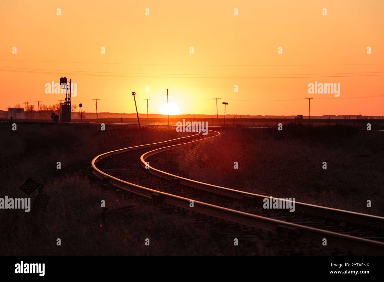 The sun is setting over a train track, casting a warm glow over the ...