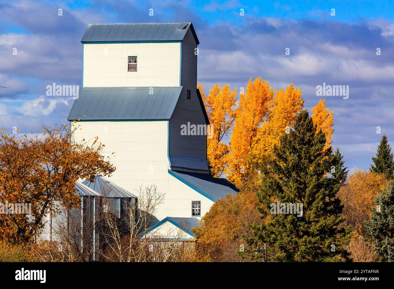 A large white building with a blue roof and a tall silo. The building ...
