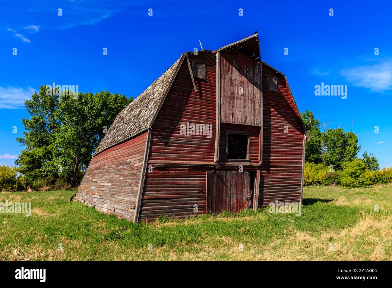 A red barn with a slanted roof sits in a field. The barn is old and has ...