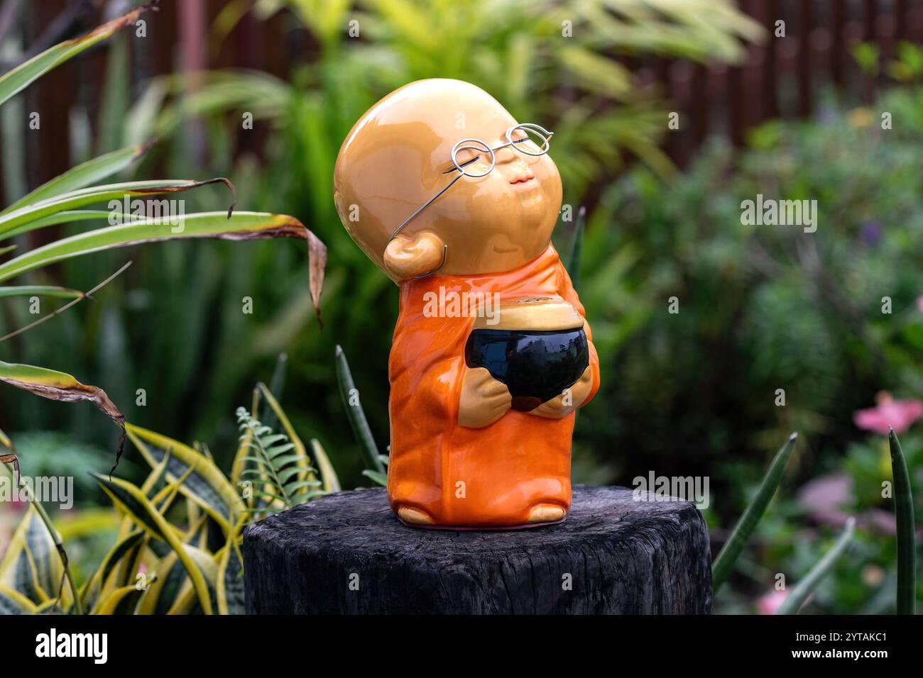 Small colored statue of Buddist monk with glasses, on a tree stump in ...