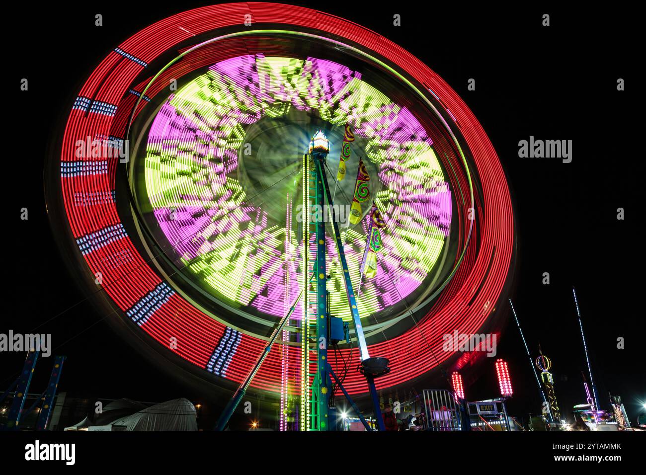 A carnival ride with a red and green wheel. The ride is lit up and ...