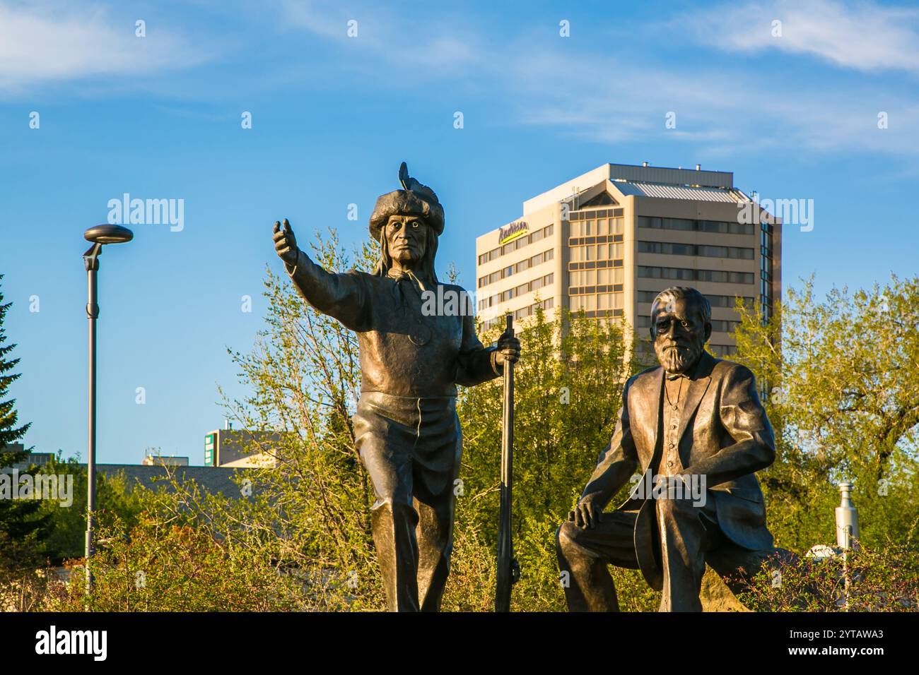 Two statues of men sitting on a bench in front of a building. One of ...