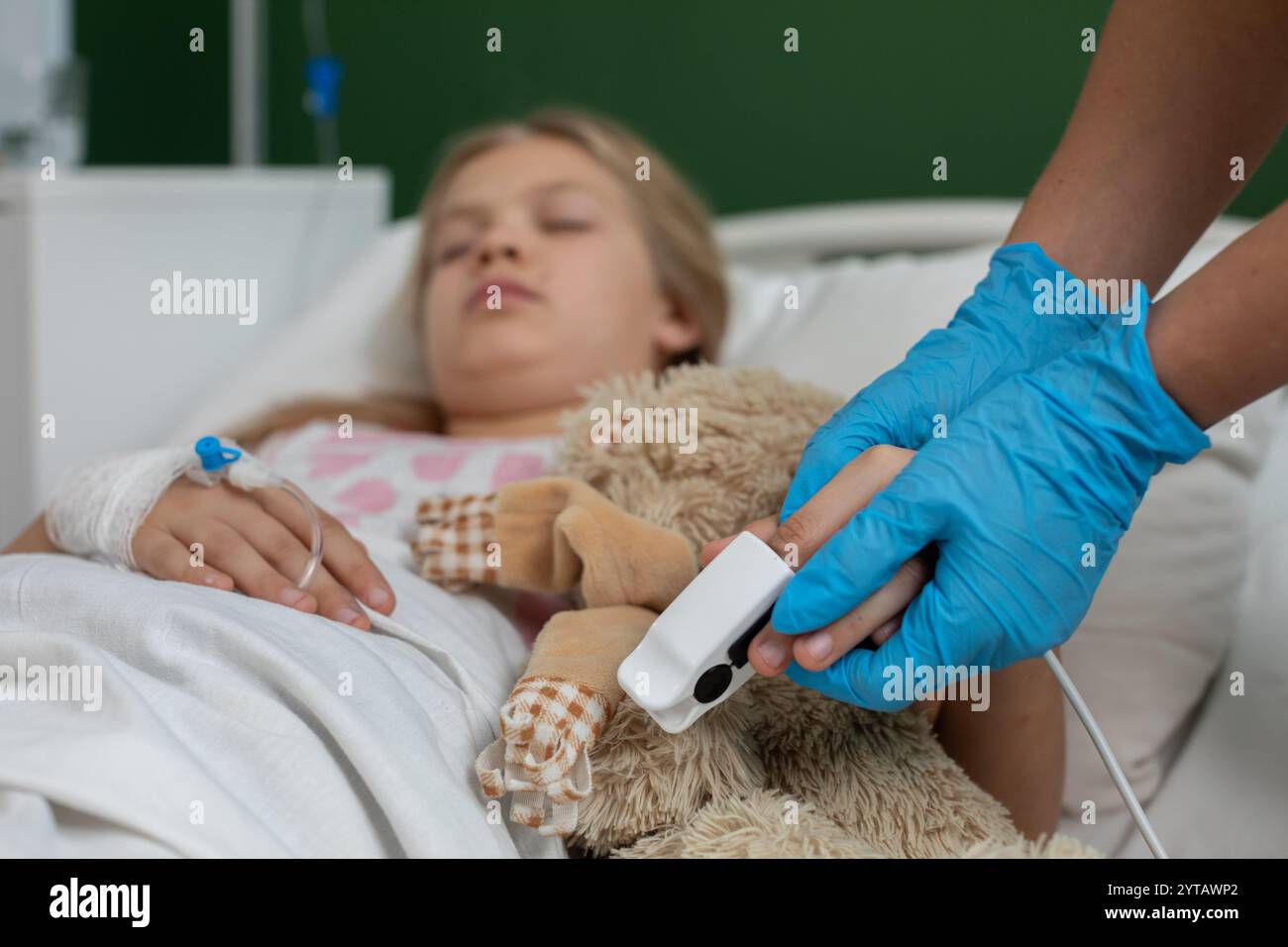 A child in a hospital bed, holding a teddy bear and connected to vital ...