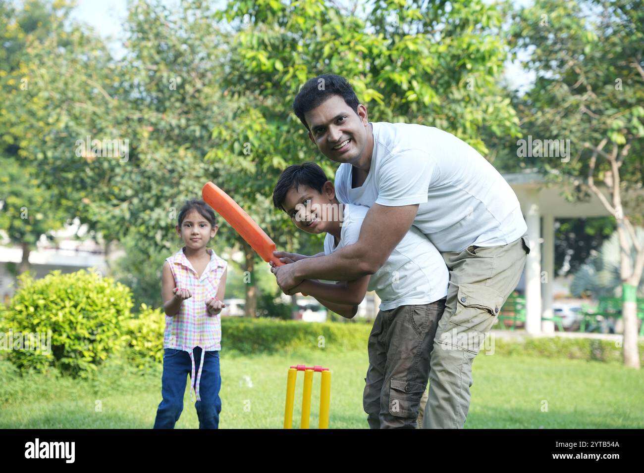 happy indian family playing cricket in park. father teaching his son to ...