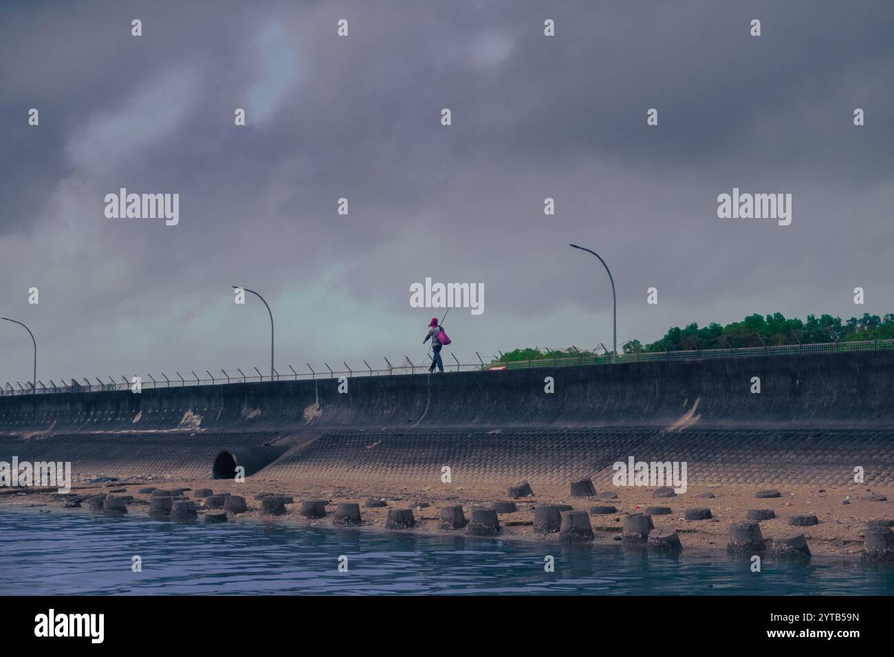 seen from a distance, a man is walking while carrying a fishing rod ...