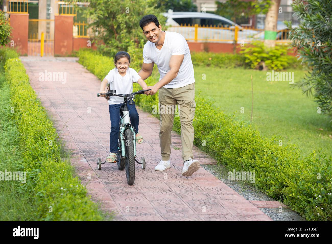 Young indian father teaching her daughter to ride bicycle in park ...