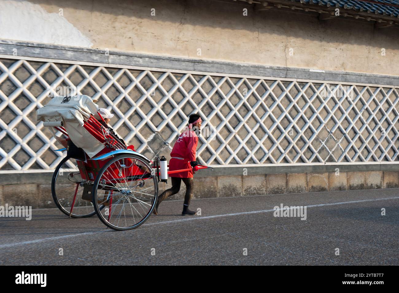 A human-powered pedicab jinrikisha with customer aboard passes a ...