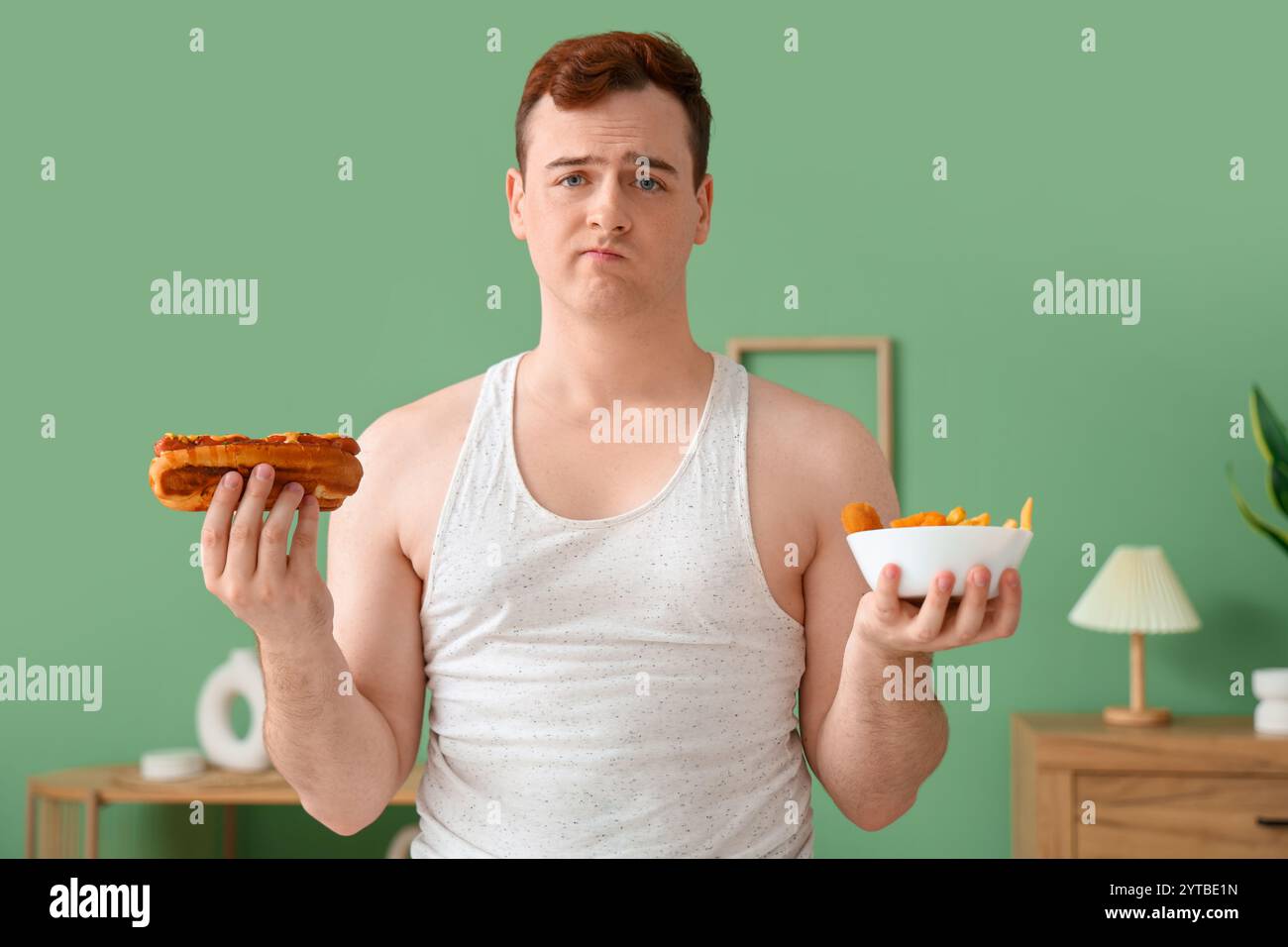 Young sad overweight man with unhealthy food at home. Weight gain ...