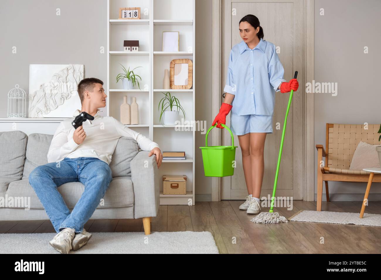 Wife mopping floor while her lazy husband playing video game at home ...