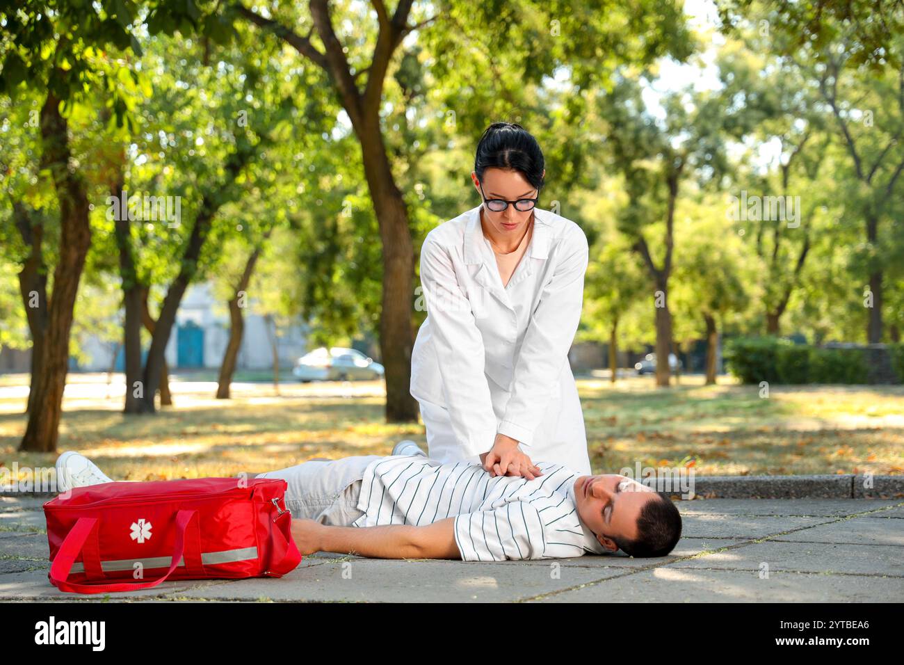 Female doctor doing CPR on unconscious man having heart attack in park ...