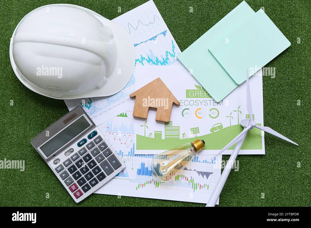 Wind turbine with light bulb, calculator, hardhat and diagrams on grass ...