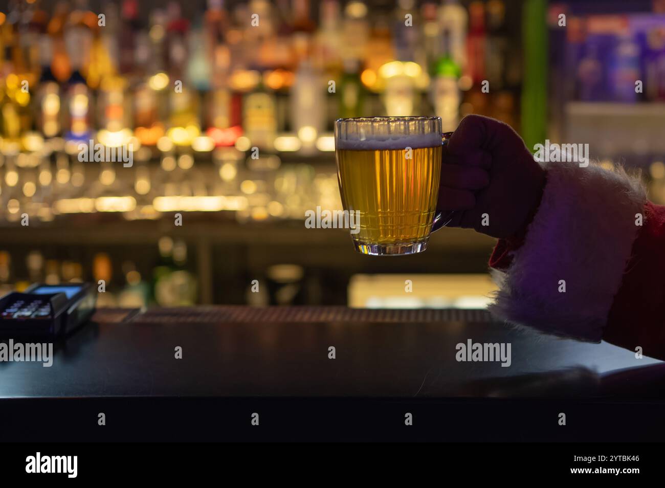 Santa Claus drinking beer at a bar. Close-up of a hand holding a mug of ...