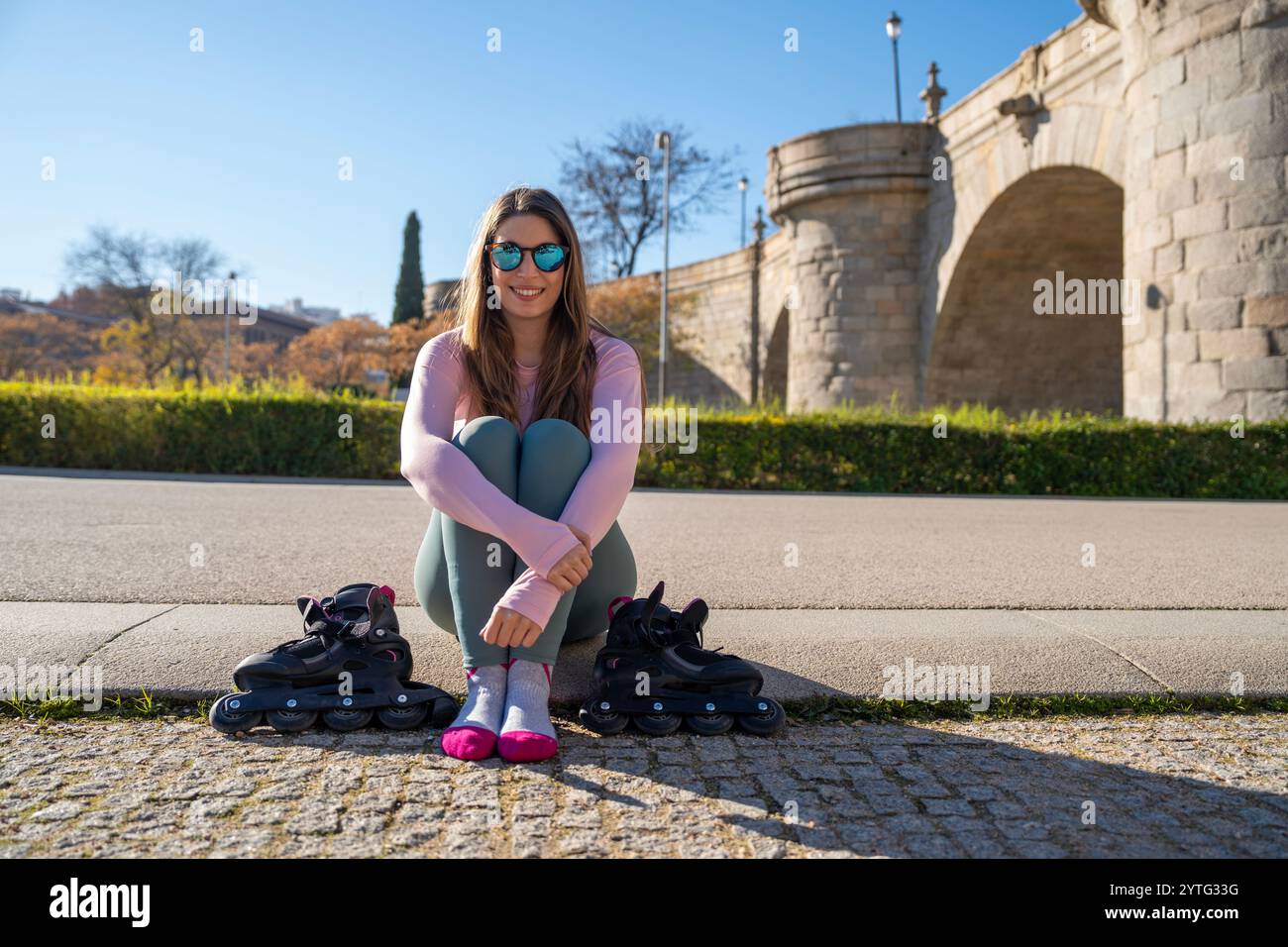 Smiling young woman resting after inline skating session in urban park ...
