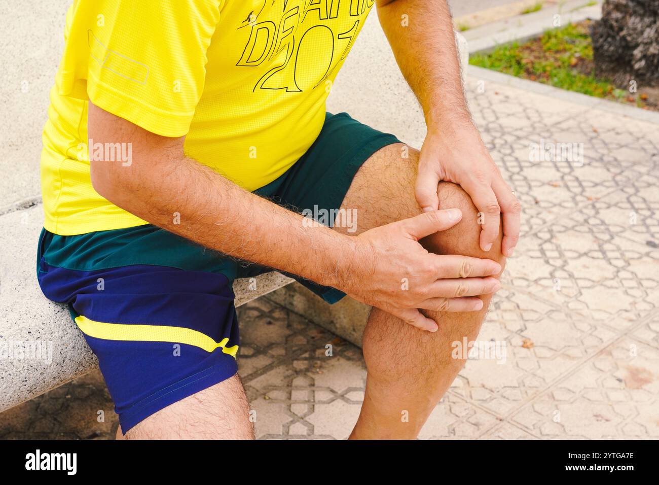 A middle aged man jogging complains of knee pain and holds his knee on ...