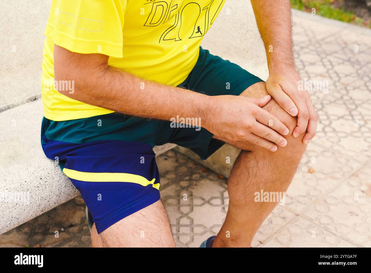A middle aged man jogging complains of knee pain and holds his knee on ...