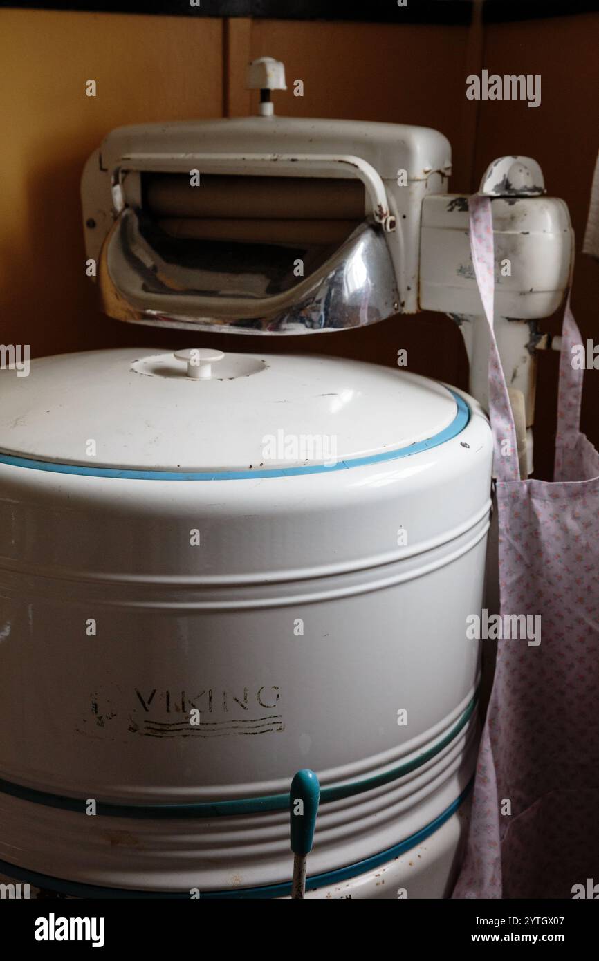 A vintage washing machine with a blue and white lid sits in a room. The ...