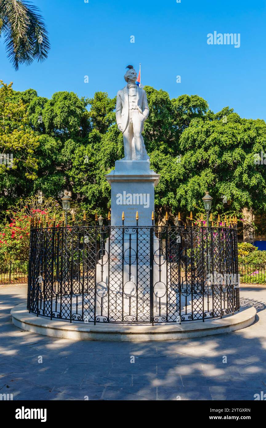 A statue of a man stands in front of a fence. The statue is white and ...