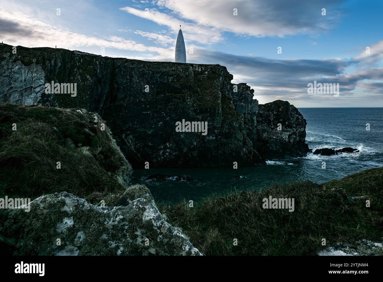 Coastal cliff scene. White conical structure atop layered dark rocks ...