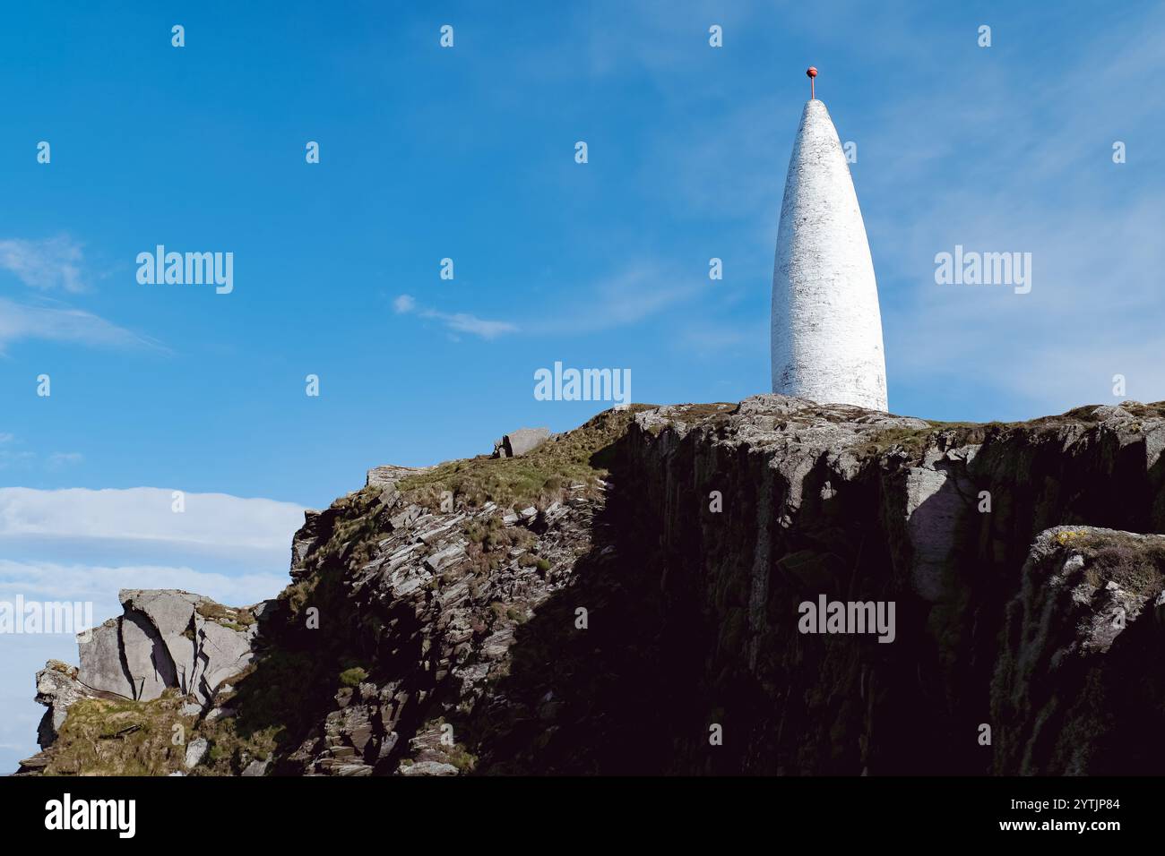 The image shows a white, pointed tower on a cliff edge. The sky above ...