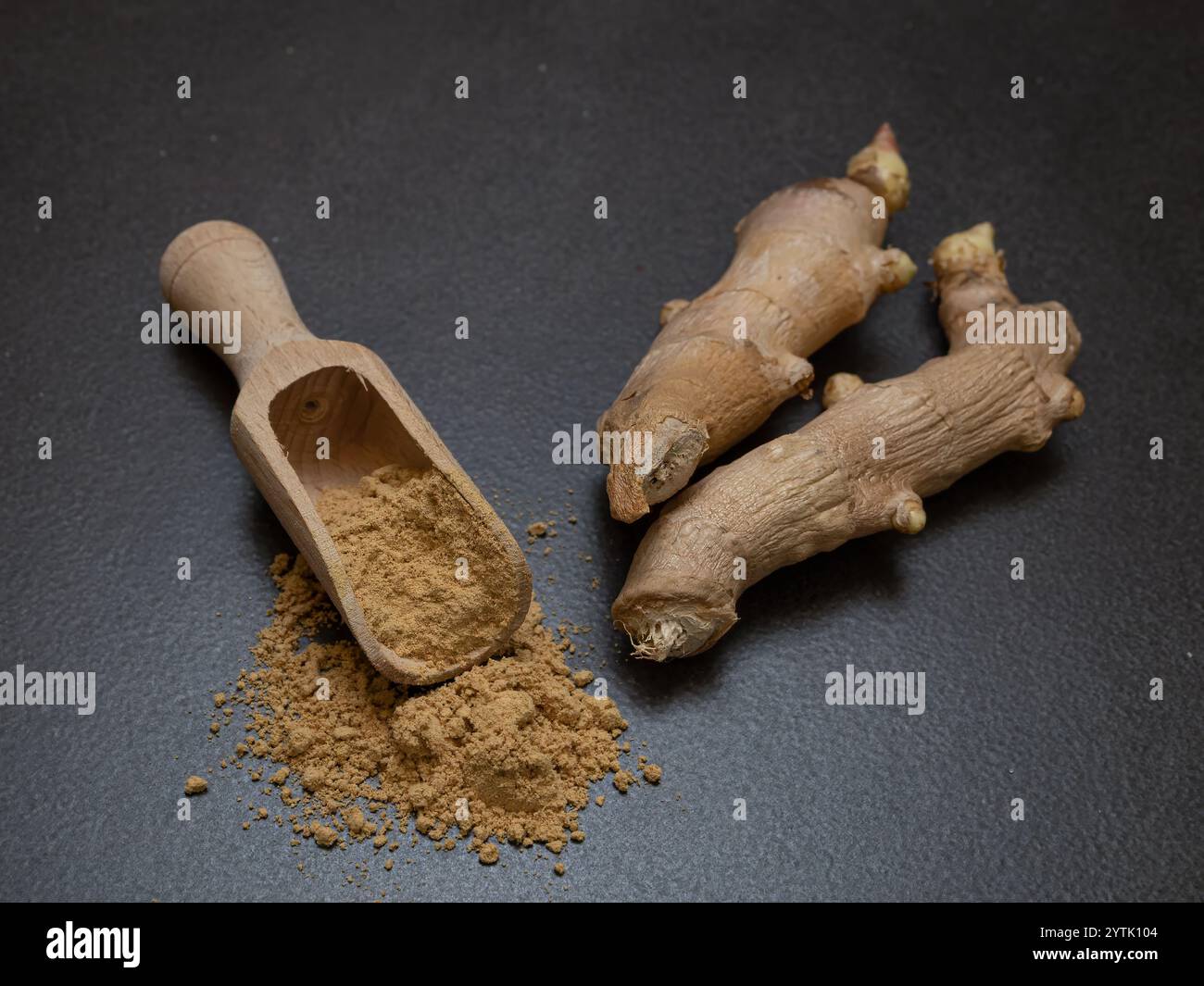 Warming ginger, root and ground with wooden spatula on dark background ...