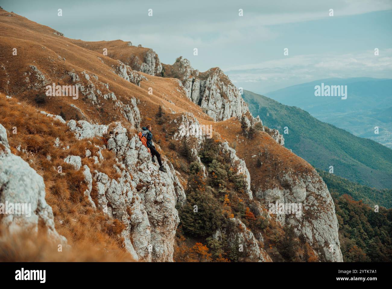Male climber stands alone on the edge of a cliff mountain top and looks ...